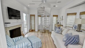 Uma sala de estar ampla com lareira, um sofá branco, um banquinho listrado, um sofá branco e uma escada em espiral.