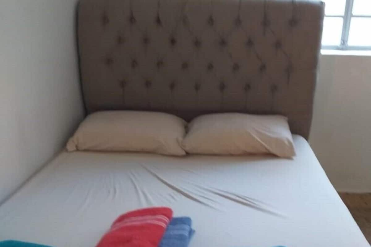 Uma cama com cabeceira estofada, duas almofadas e um cobertor azul.