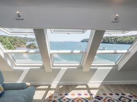 Quarto com claraboias e vista para uma baía com barcos.