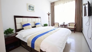 Quarto de hotel com cama, televisão, cadeira, mesa pequena e janela com cortinas.