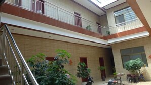 Um edifício com vários andares, uma escadaria central, varandas e áreas de estar ao ar livre com plantas em vasos.