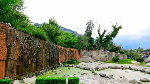 Um caminho de pedra que leva a uma escadaria, cercado por vegetação e um muro decorativo.