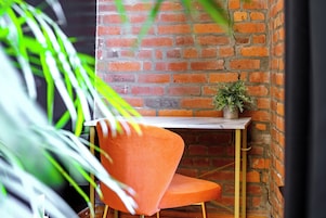 Um canto com parede de tijolos, uma mesa, uma cadeira e um vaso de planta.