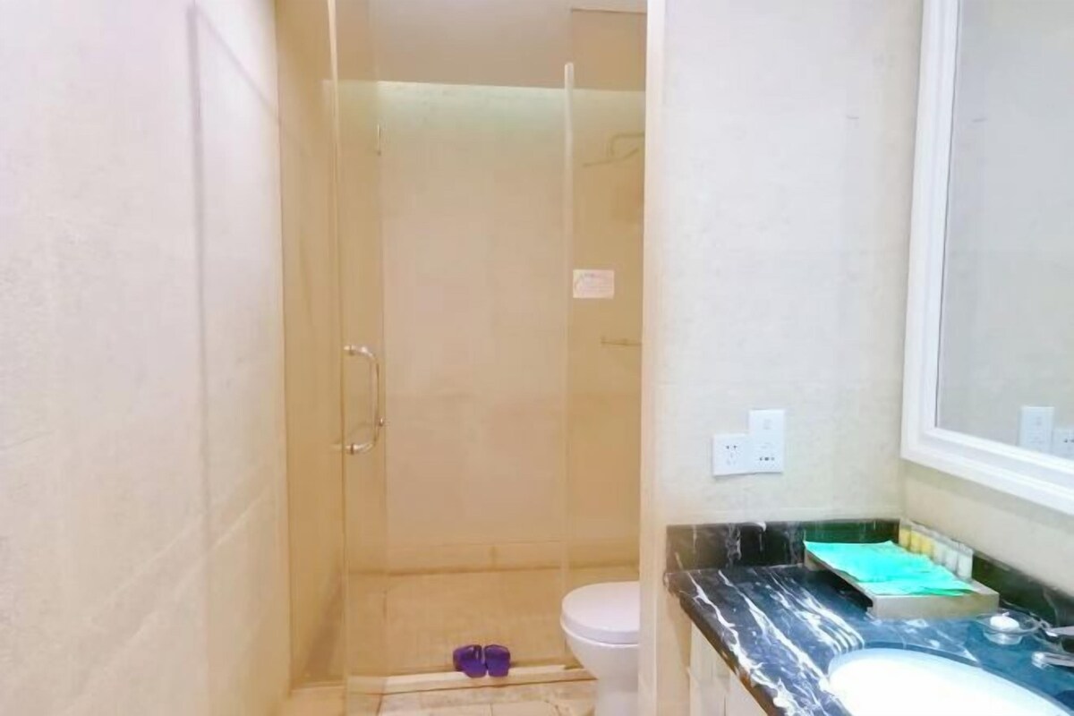 Casa de banho com cabine de duche em vidro, sanita branca e lavatório com bancada de mármore.