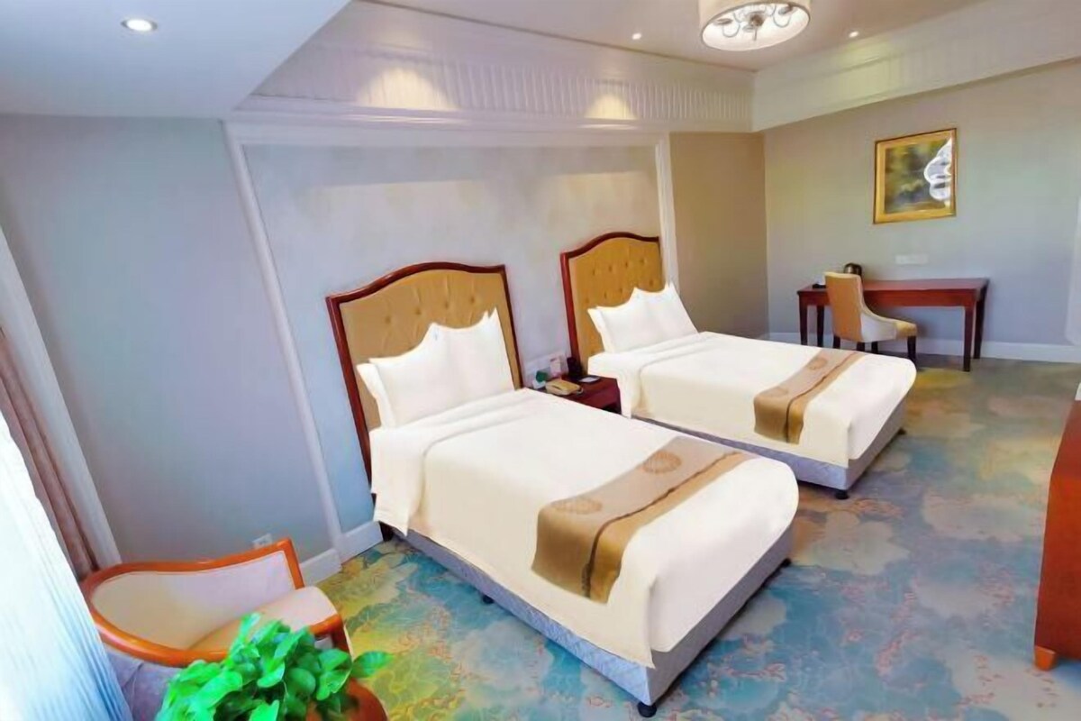 Quarto de hotel com duas camas, uma escrivaninha, uma cadeira e um quadro na parede.