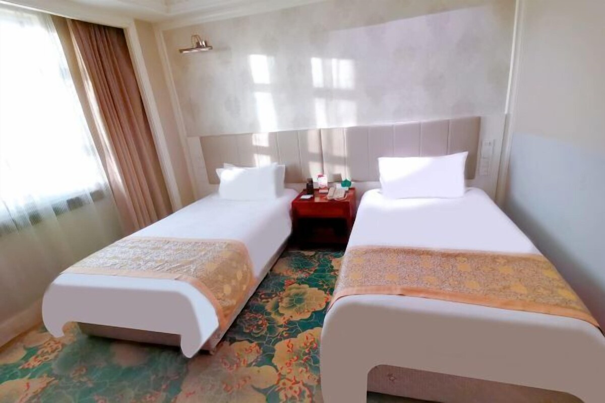 Quarto de hotel com duas camas, uma mesinha de cabeceira e uma janela com cortinas.