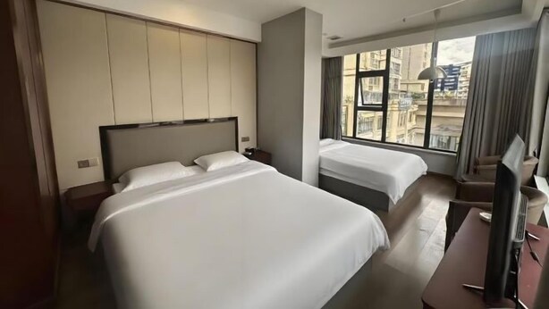 Quarto de hotel com duas camas, uma escrivaninha, uma TV e uma janela grande com vista para a cidade.