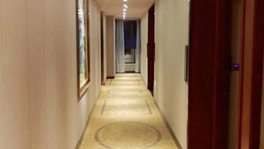 Um corredor comprido e estreito, com carpete estampado e uma porta à direita.