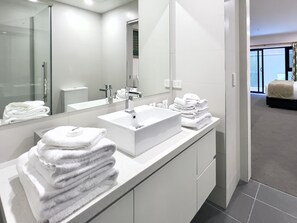 Casa de banho moderna com um espelho grande, lavatório branco e toalhas empilhadas.