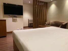 Quarto de hotel com uma cama grande, televisão fixada na parede, uma cadeira de madeira e um painel de madeira.