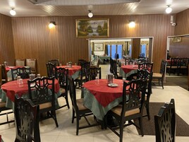 Restaurante com mesas redondas cobertas por toalhas vermelhas, cadeiras de madeira e uma parede de painéis de madeira com um quadro.