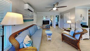 Uma sala de estar com sofá, duas cadeiras de vime, uma mesinha e um ventilador de teto.