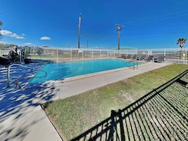 Piscina com placa de proibição de mergulho, cercada por uma grade branca e área gramada com espreguiçadeiras.