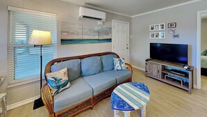 Uma sala de estar com sofá, televisão, luminária e uma mesinha.