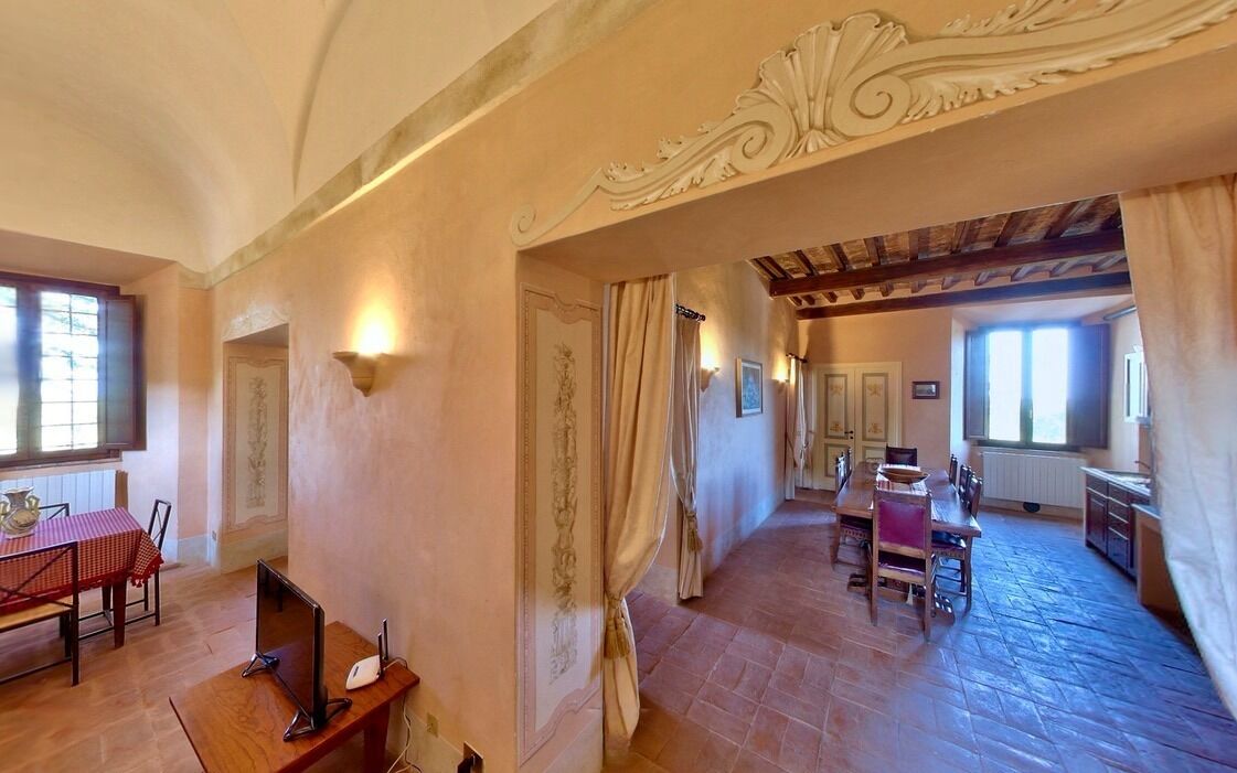 Um quarto espaçoso com piso de madeira, área de jantar com mesa e cadeiras, e uma televisão.