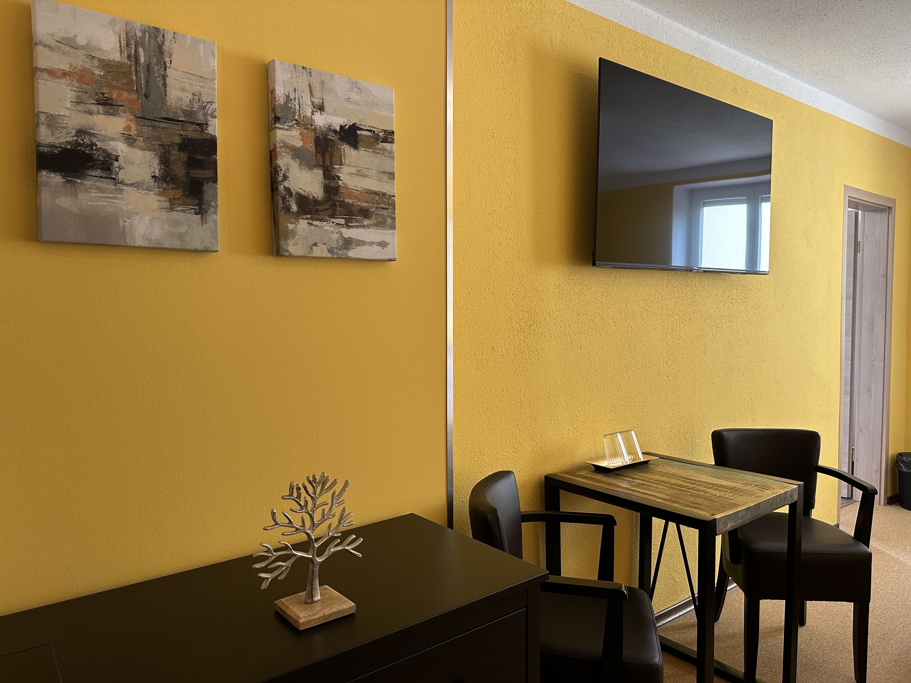 Uma sala de jantar com mesa e cadeiras, uma árvore decorativa e arte abstrata nas paredes.