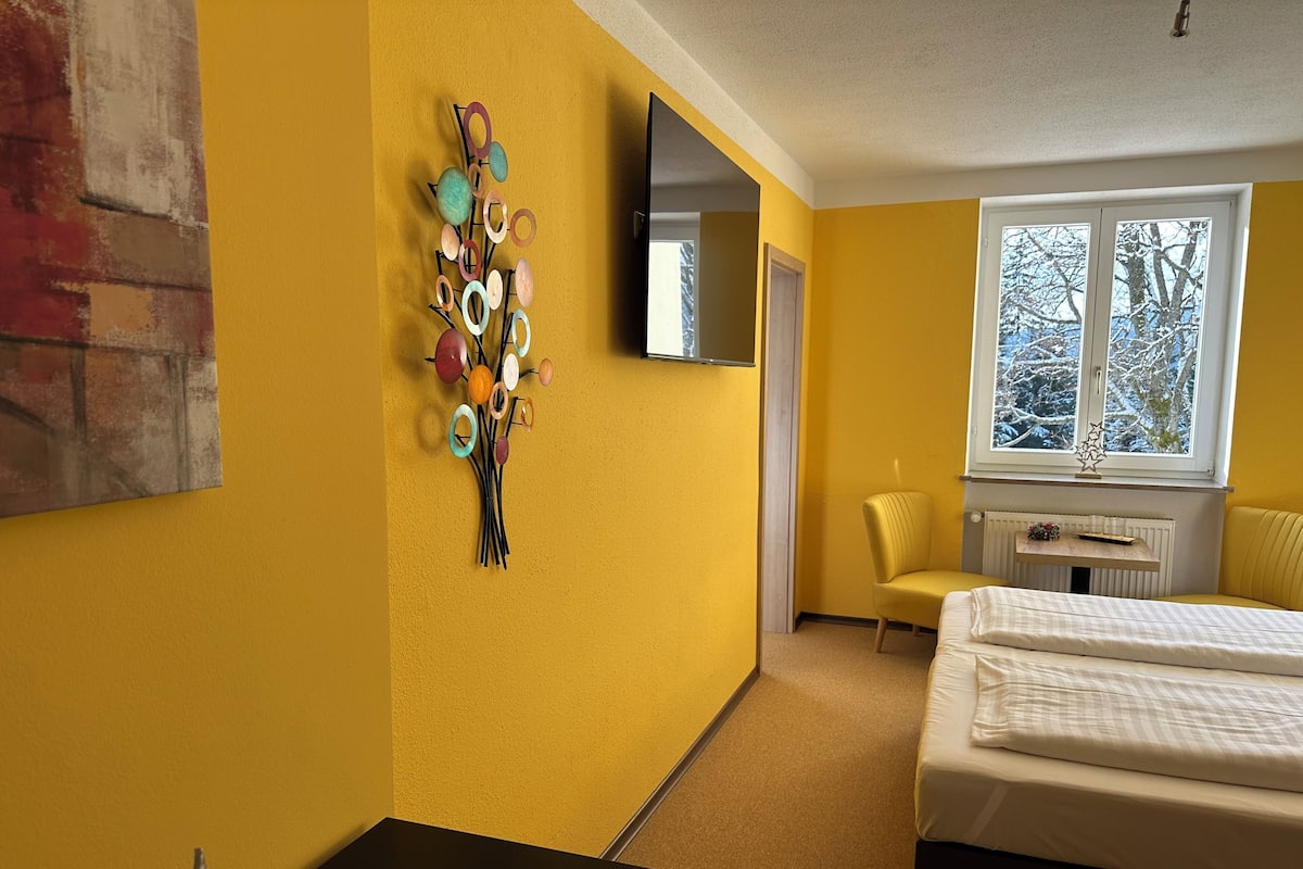 Quarto com cama, cadeira, escrivaninha, televisão e decoração na parede.