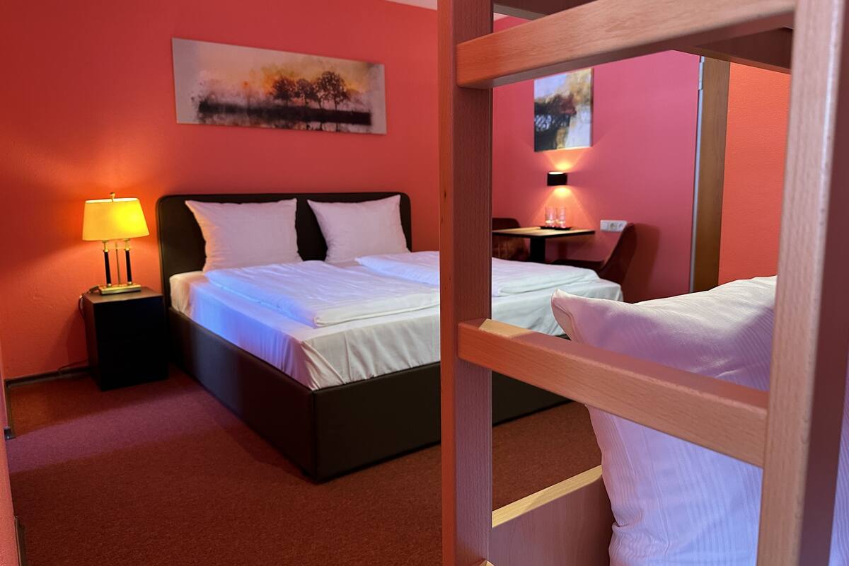 Quarto de hotel com cama, mesa de cabeceira com abajur, quadro na parede e espelho refletindo o ambiente.