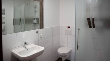 Uma casa de banho moderna com uma pia branca, sanita e cabine de duche em vidro.