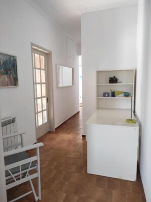 Um corredor com um banco branco, um armário branco e uma prateleira com diversos objetos.