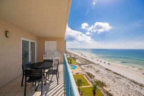 Uma varanda com mesa e cadeiras, com vista para uma praia que inclui piscina e cerca.