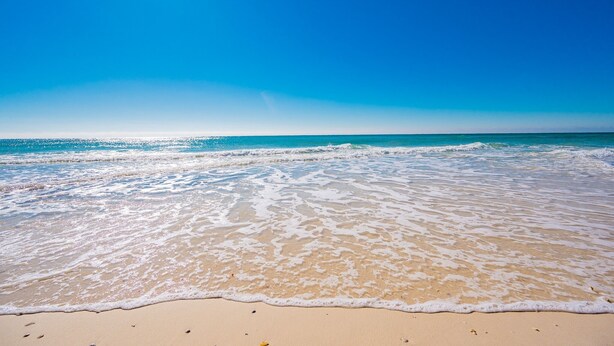 Uma praia com águas azul-claras e areal arenoso.