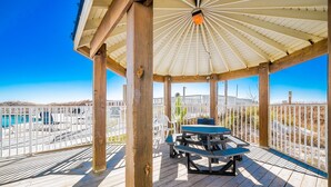 Um deck de madeira com um gazebo, mesa de piquenique e vista para a piscina.