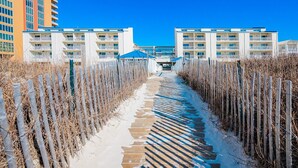 Caminho que leva a um hotel à beira-mar, com várias varandas e um céu azul límpido.