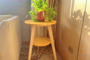 Canto com uma pequena mesa de madeira, um vaso de planta, uma cadeira branca e um tapete estampado.