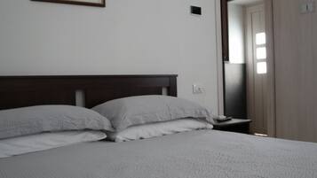 Quarto com cama, almofadas, mesa de cabeceira, quadro na parede e porta que dá para outro cômodo.