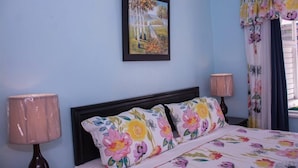 Quarto com cama, almofadas florais, um quadro na parede e cortinas.