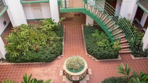 Um átrio com vários níveis, uma escadaria central e bastante vegetação, com piso em azulejos.