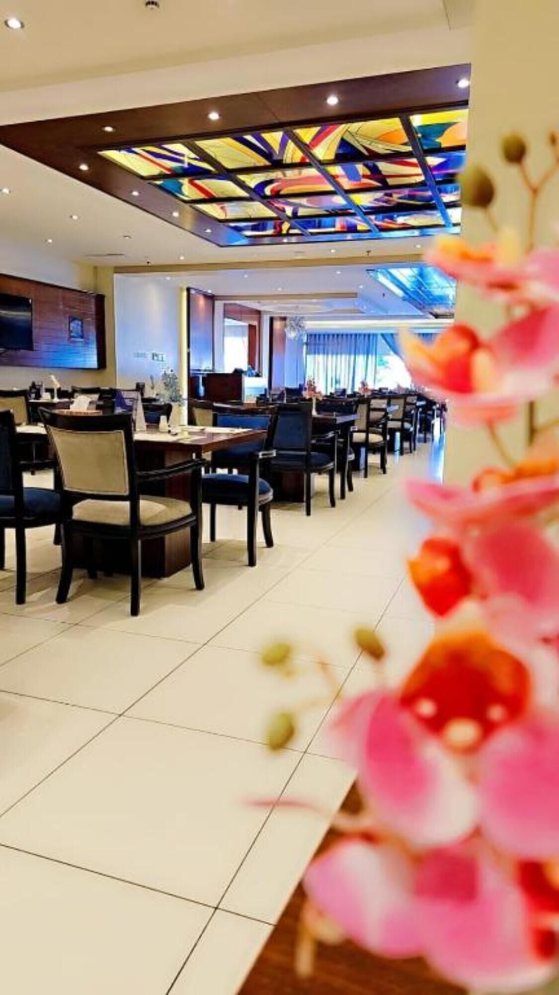 Um saguão de hotel com um balcão de recepção extenso, diversas áreas de estar e um design de teto colorido.