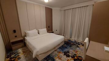 Quarto de hotel com cama grande, mesa de cabeceira, guarda-roupa e cortina.