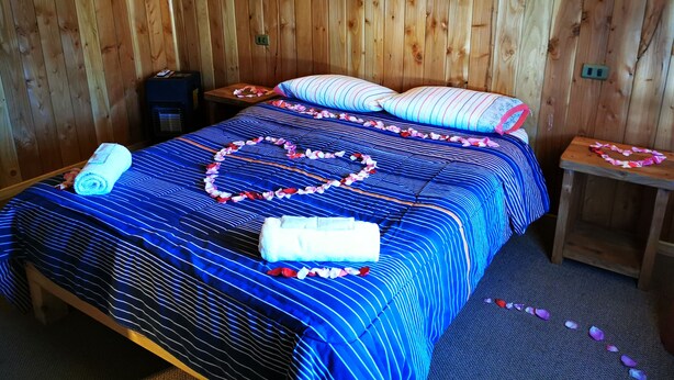Quarto com painéis de madeira, uma cama, duas mesas de cabeceira e luminárias na parede.