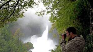 Uma pessoa fotografando uma cascata em meio a vegetação exuberante.