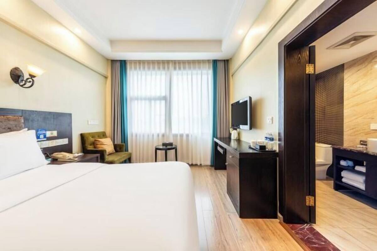 Quarto de hotel com cama, escrivaninha, cadeira, televisão e banheiro.