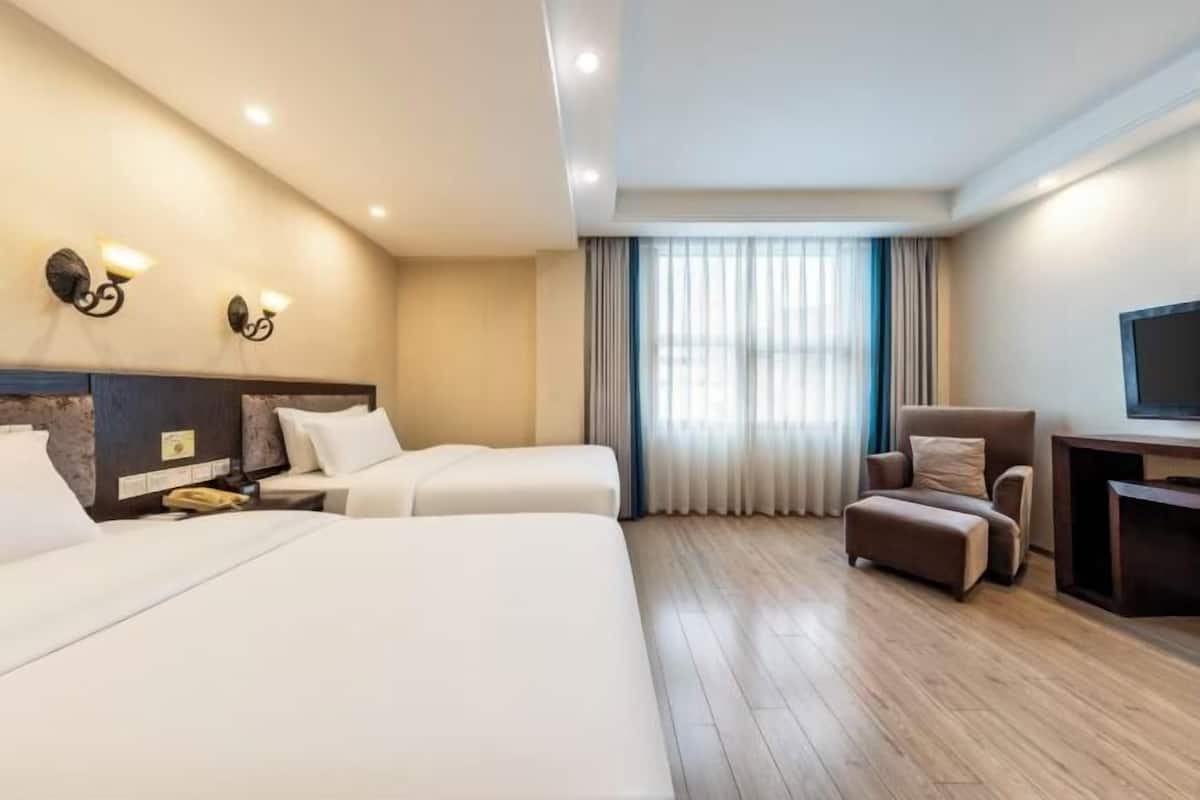 Quarto de hotel com duas camas, um sofá, uma televisão e uma escrivaninha.