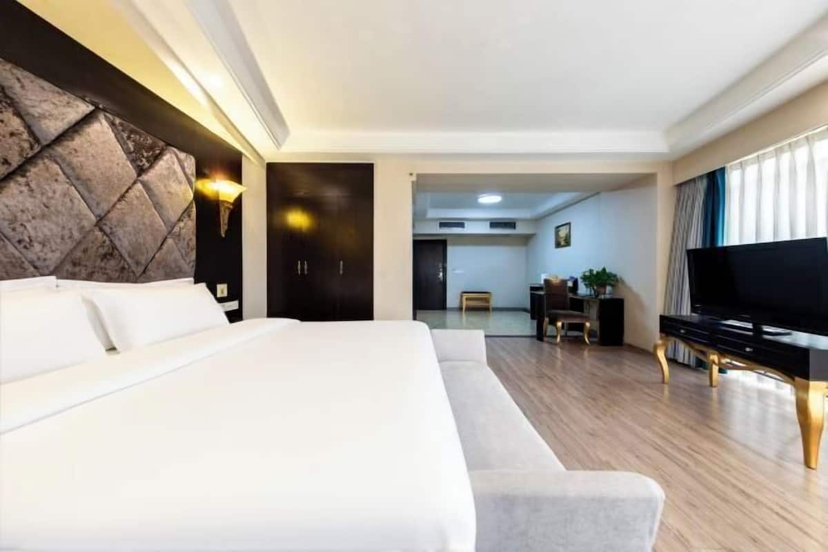 Quarto de hotel com uma cama grande, televisão, secretária e área de estar.