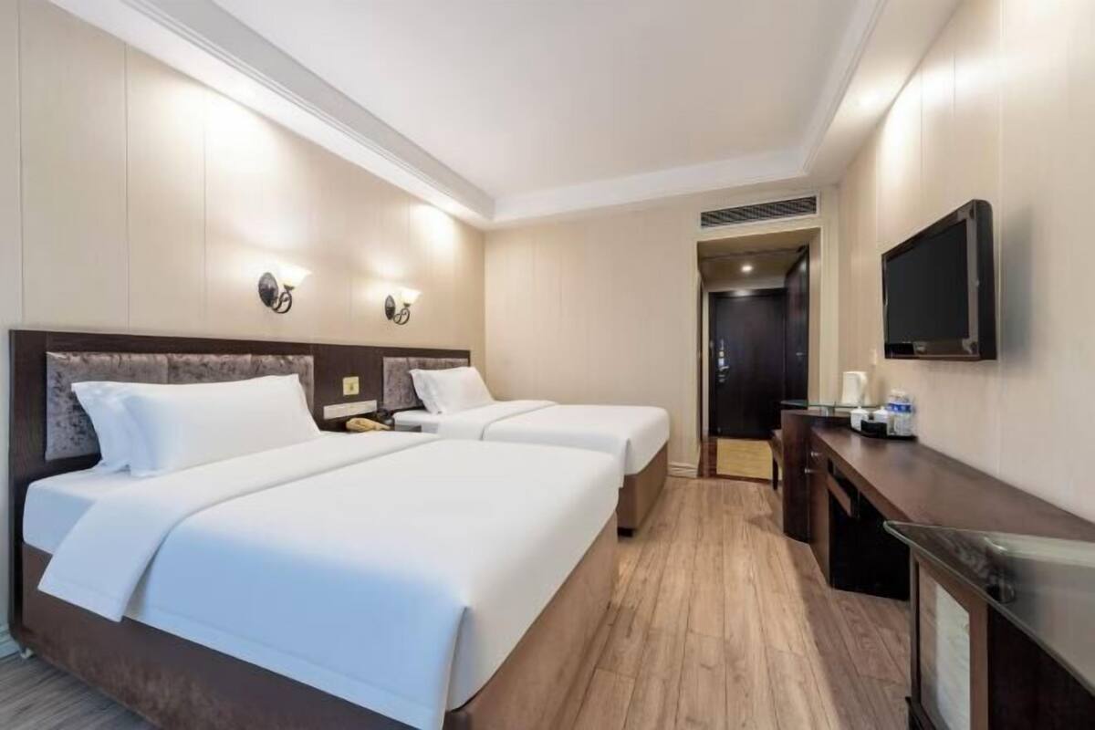 Quarto de hotel com duas camas, uma escrivaninha, uma televisão de tela plana e uma porta que dá para outro quarto.