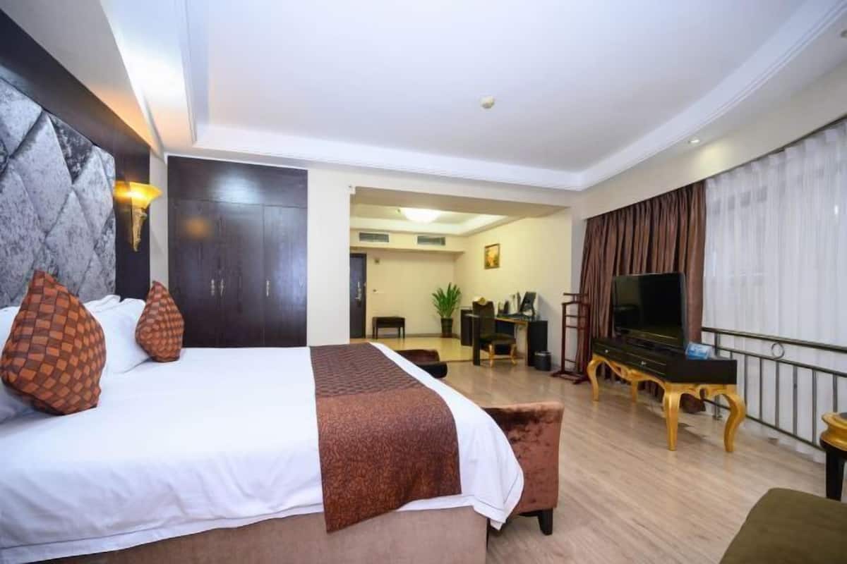 Quarto de hotel com uma cama grande, uma escrivaninha, uma televisão e um espaço de estar.