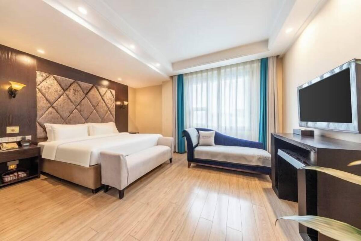 Quarto de hotel com cama, sofá, televisão e secretária.