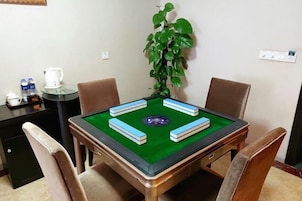 Quarto com mesa de bilhar, quatro cadeiras, cafeteira, garrafas de água e planta em vaso.