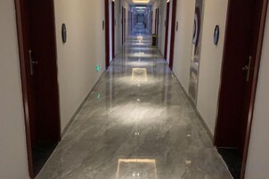 Corredor longo e estreito de um hotel, com portas de ambos os lados, dando acesso aos quartos.