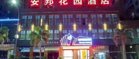 Um hotel com uma placa vermelha chamativa, vários andares e uma entrada bem iluminada.
