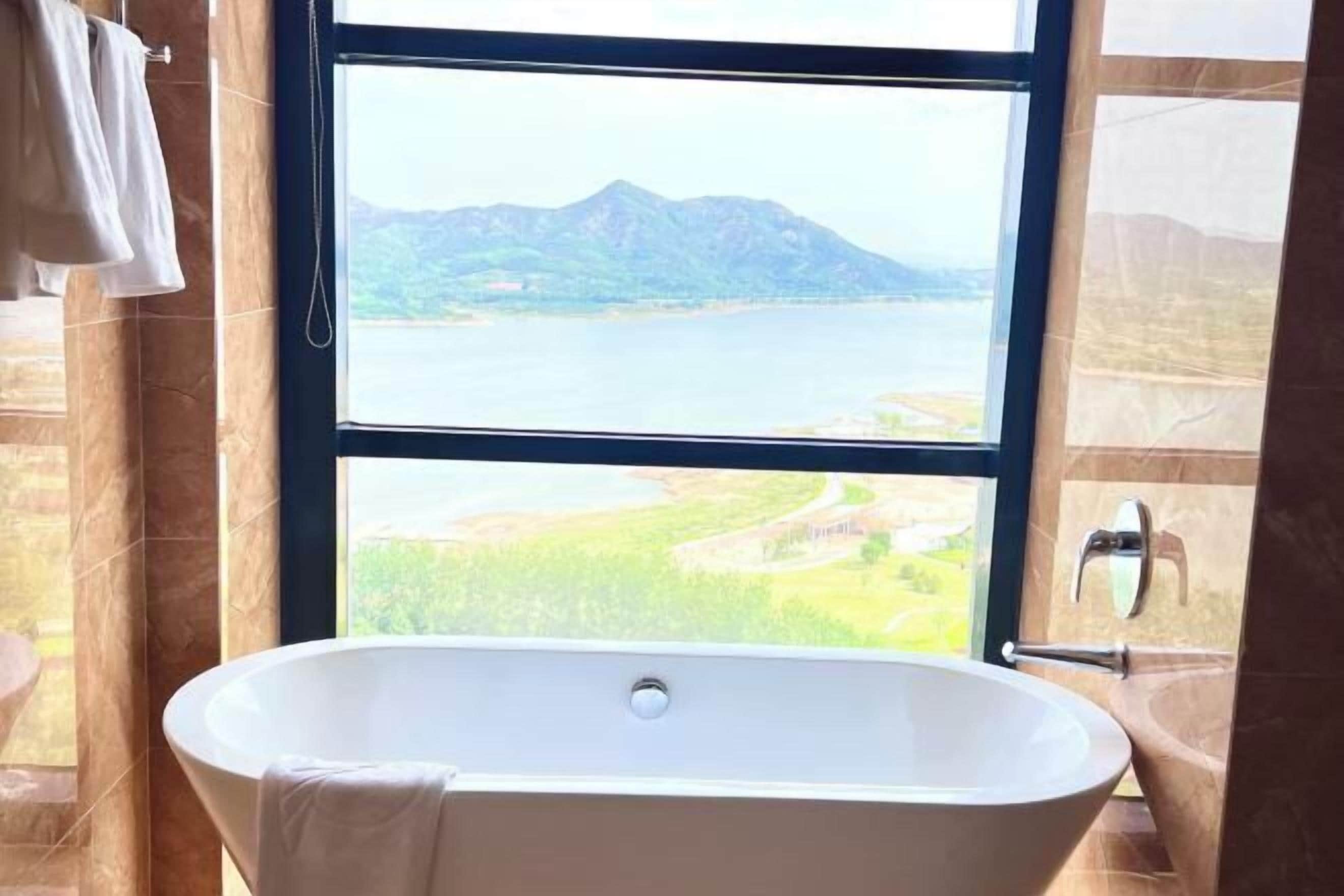 Um banheiro com banheira livre, uma janela com vista para um lago e montanhas, e um porta-toalhas.