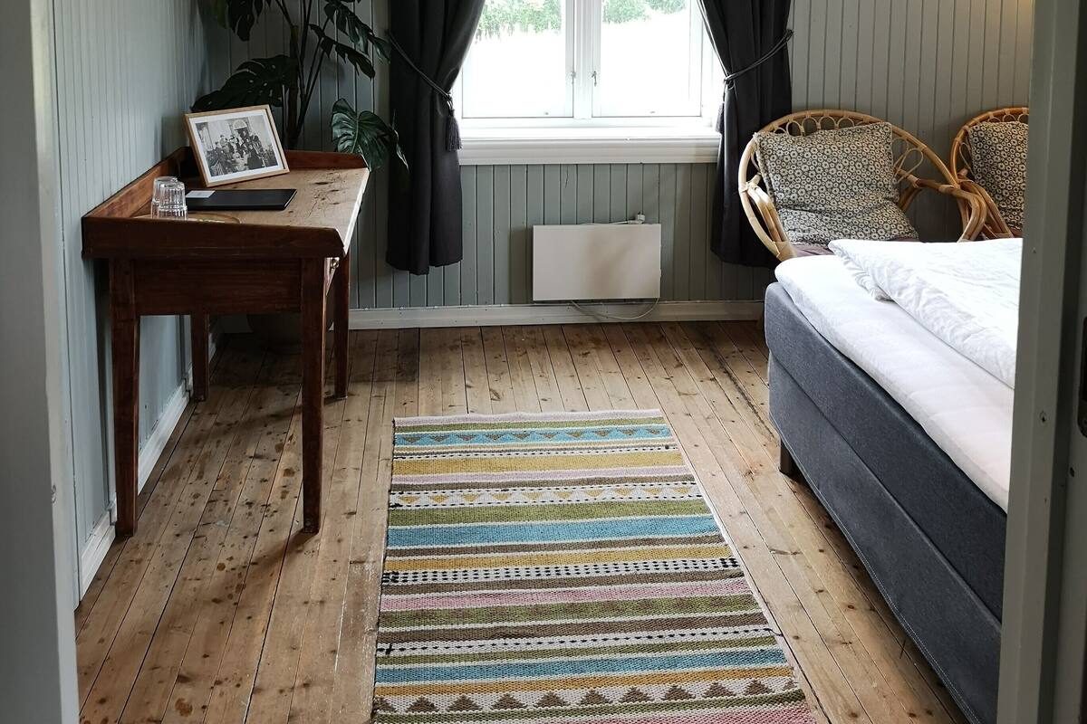 Quarto com cama, escrivaninha com planta, cadeira e janela com cortinas.
