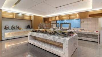 Uma área de buffet com diversas estações de serviço, bancada de mármore e iluminação pendente.