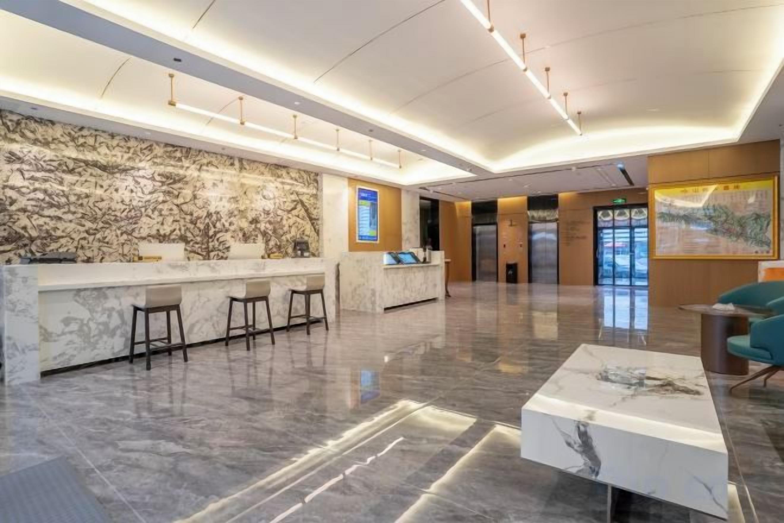Um hall de hotel com balcão de recepção de mármore, banquetas de bar e uma grande obra de arte na parede.