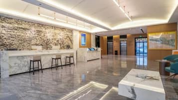 Um hall de hotel com balcão de recepção de mármore, banquetas de bar e uma grande obra de arte na parede.